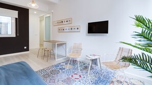 Uma sala de estar moderna com um sofá, uma mesa de centro, duas poltronas, uma TV e quadros nas paredes.