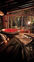 Quarto acolhedor com hidromassagem, móveis de madeira e vista para árvores através de grandes janelas.