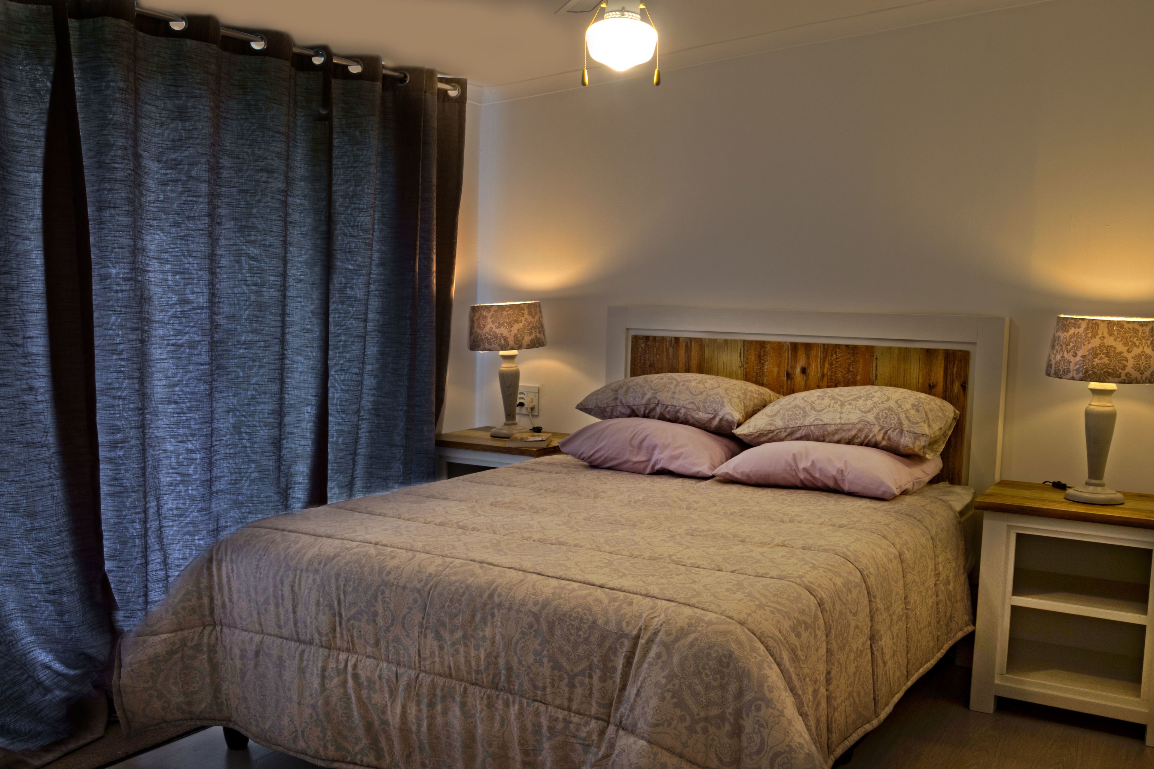 Cama bem arrumada com colcha estampada, duas luminárias de cabeceira e mesa de cabeceira com abajur.
