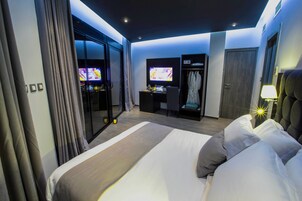 Quarto de hotel moderno com uma cama grande, uma escrivaninha com computador, televisão e guarda-roupa.