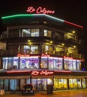 Um edifício de vários andares com letreiros iluminados para 'Glacier', 'Pizza' e 'Café'.