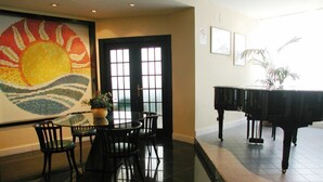 Uma sala de jantar com piano, um grande mural na parede e um vaso de planta.