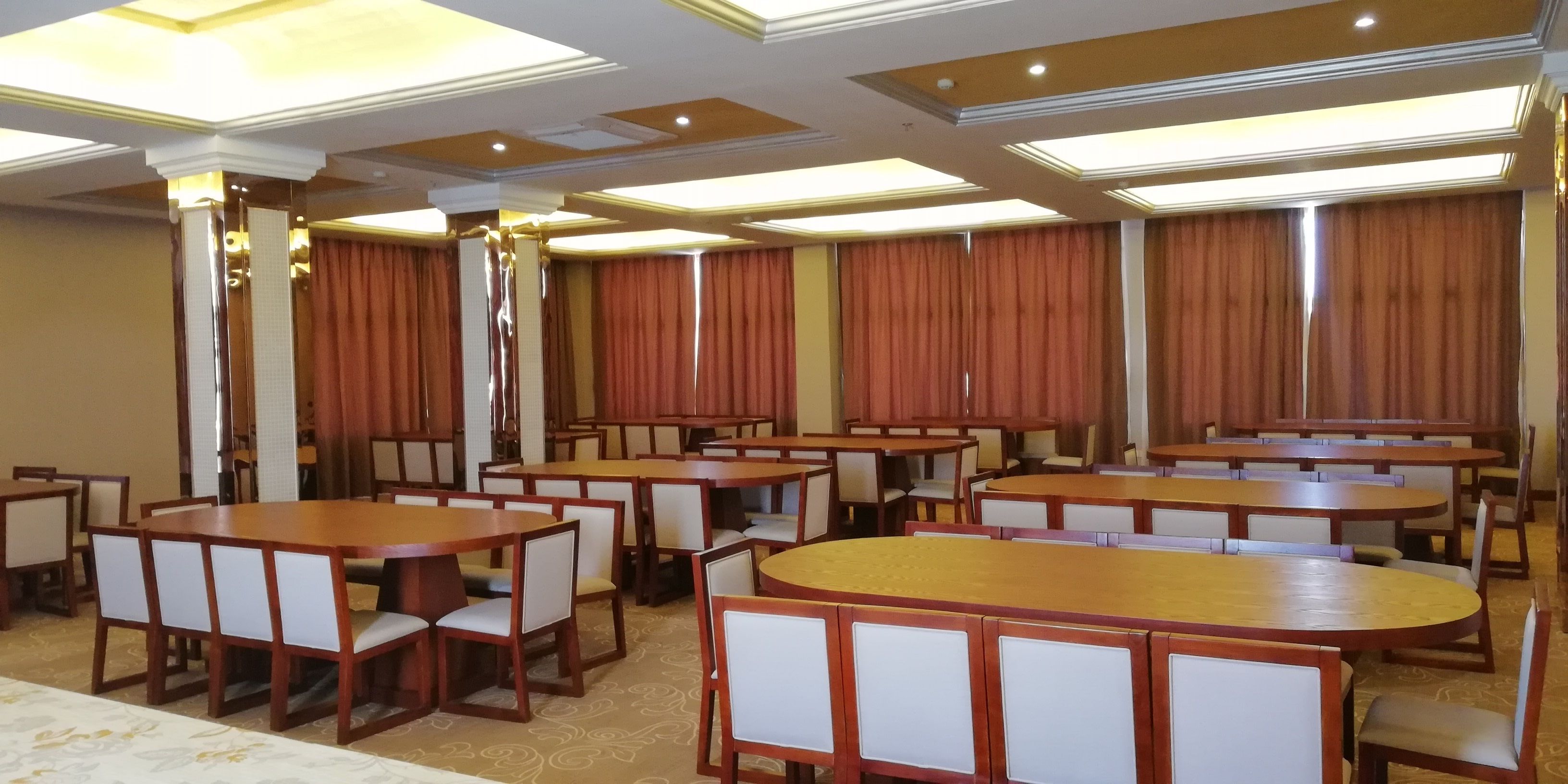 Quarto de hotel com várias mesas redondas e cadeiras, uma cama grande e uma janela com cortinas.