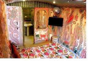 Quarto com cama, televisão, ventoinha e banheiro visível por uma porta aberta.