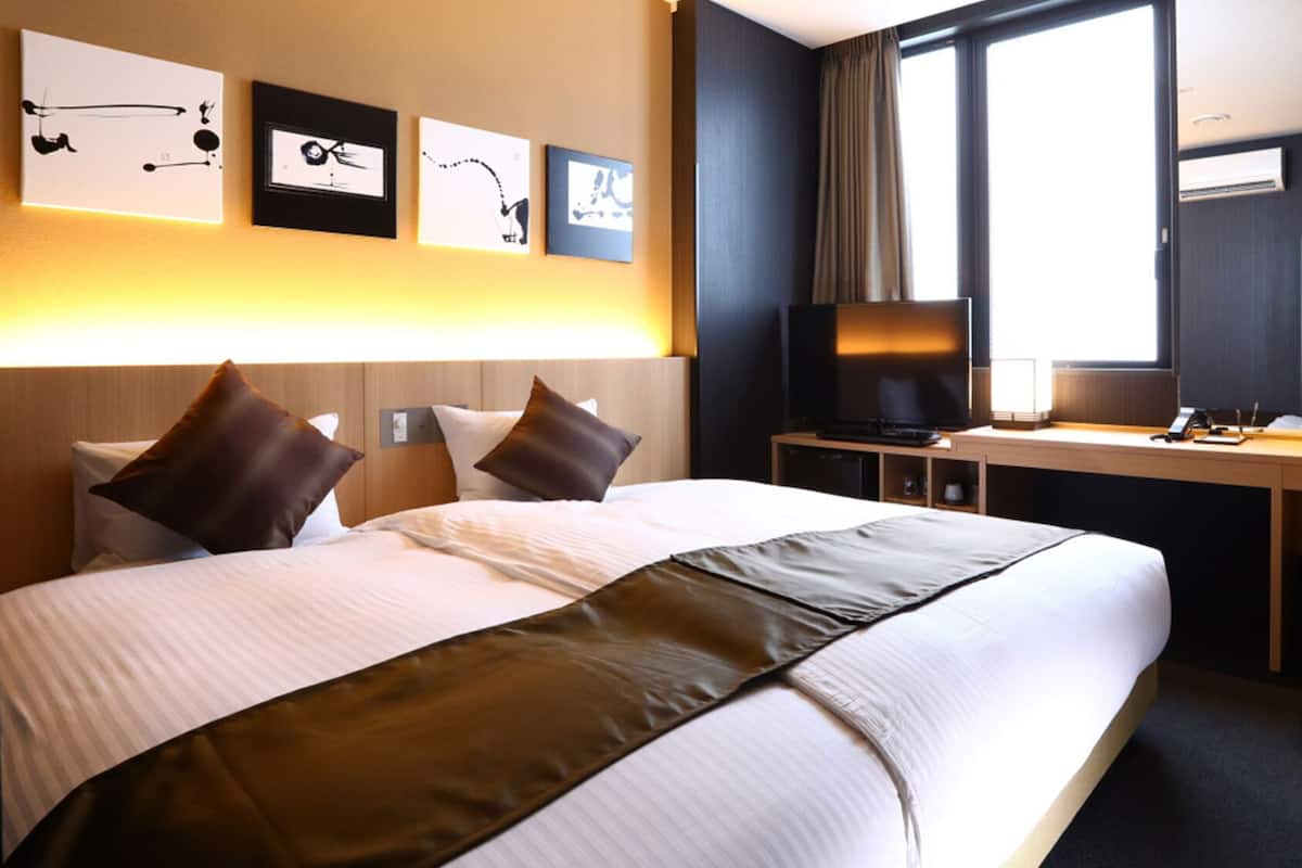 Quarto de hotel com uma cama grande, uma escrivaninha, televisão e obras de arte na parede.