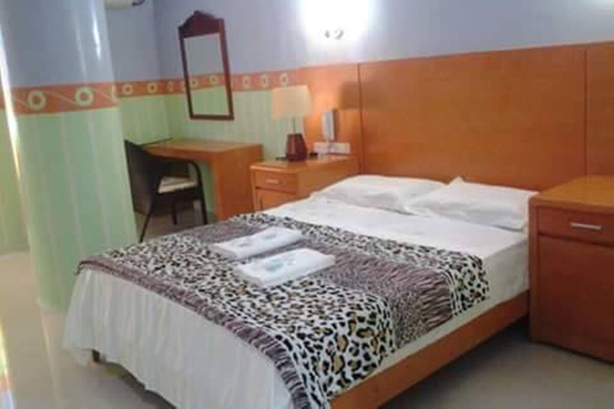 Quarto com cama, escrivaninha, cadeira e mesa de cabeceira.