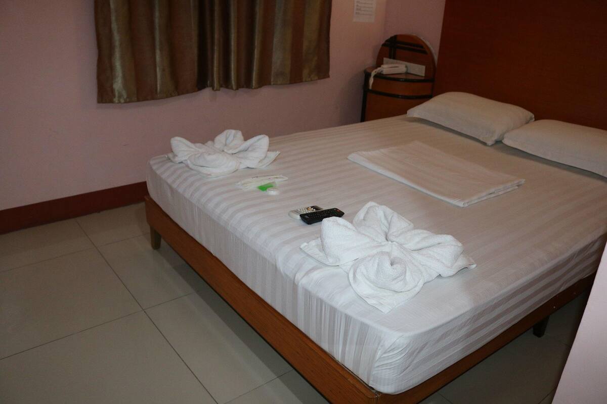 Quarto de hotel com uma cama de solteiro, mesa de cabeceira e janela com cortinas.