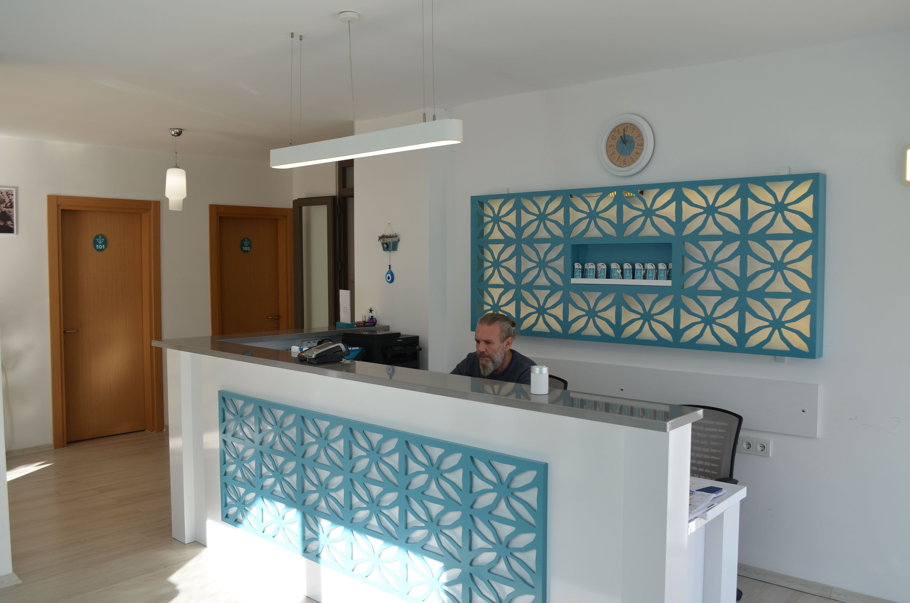 Uma área de recepção com design moderno, incluindo um balcão de atendimento, um painel decorativo e um relógio.