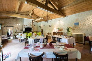 Uma sala de jantar rústica com paredes de pedra, vigas de madeira e várias mesas preparadas para refeições.