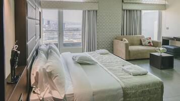 Quarto de hotel moderno com uma cama grande, um sofá, uma mesa de centro e vista para a cidade.