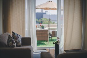 Quarto com sofá, uma orquídea em vaso e vista para um pátio externo com mesa, cadeiras e guarda-sol.