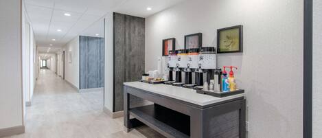 Corredor de hotel com estação de café, obras de arte emolduradas e um longo hall.
