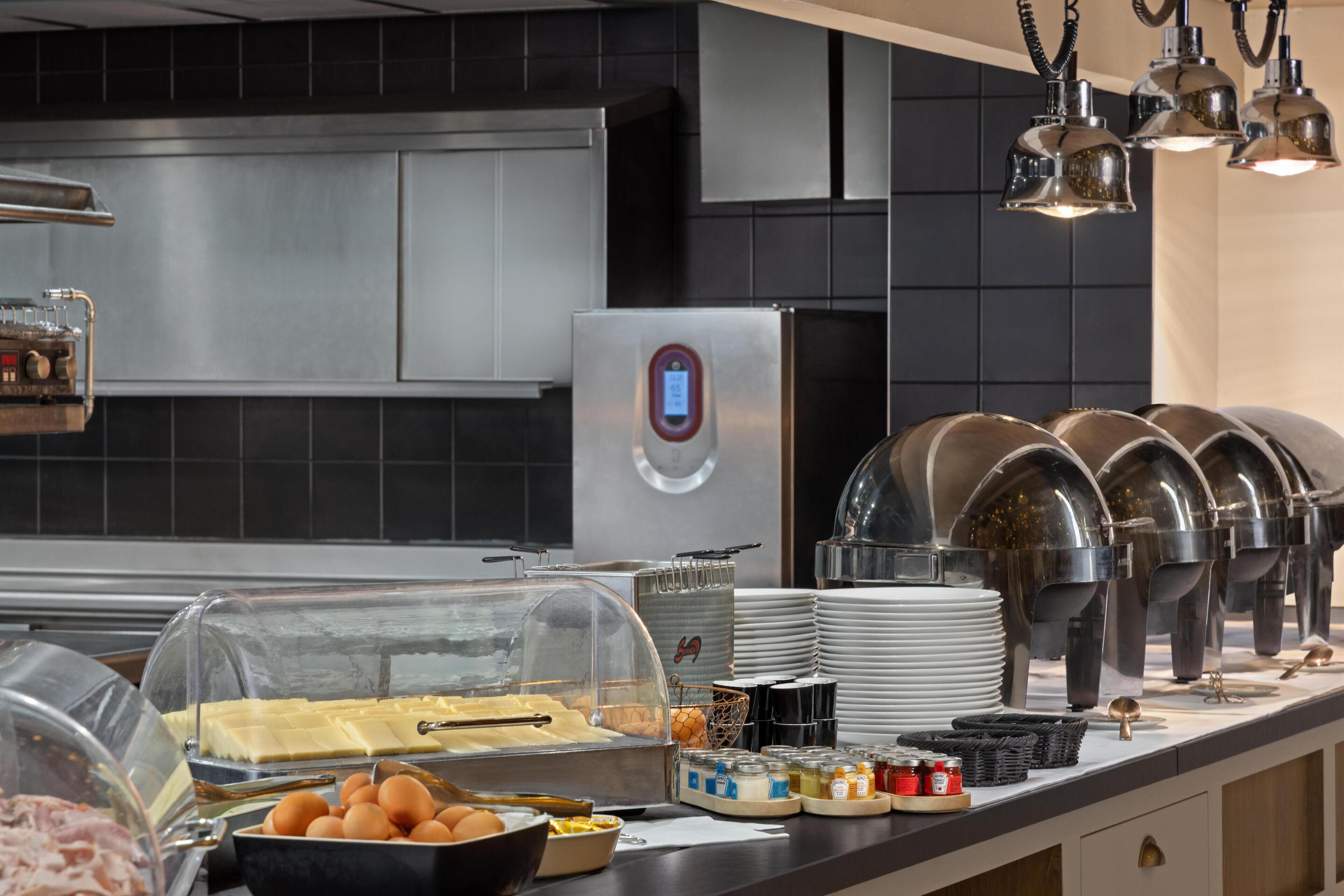 Disposição de buffet com diversos alimentos, incluindo ovos, queijo e acompanhamentos, dispostos sobre um balcão com o cenário de uma cozinha moderna.
