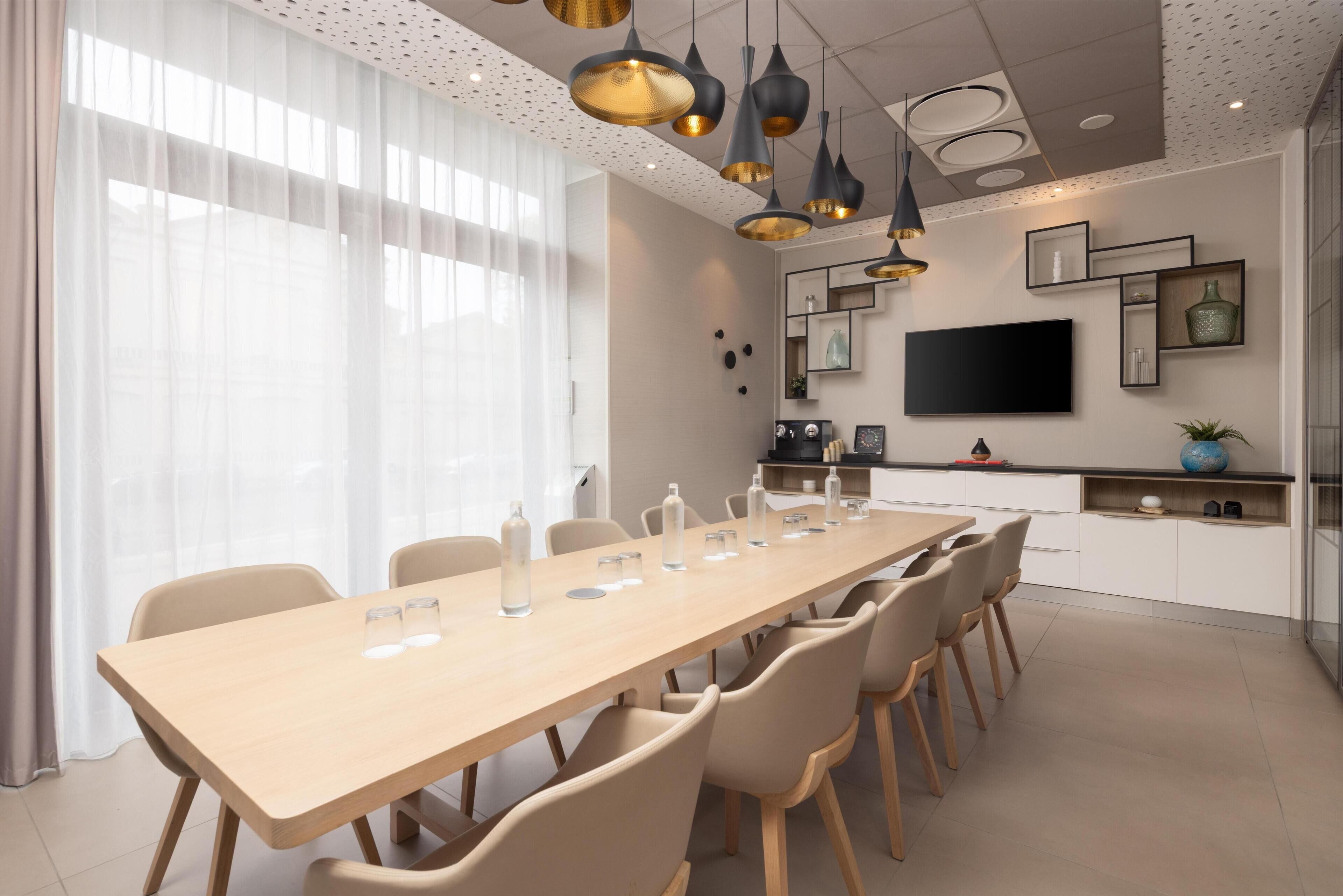 Uma sala de jantar moderna com uma mesa comprida, cadeiras e iluminação pendente.