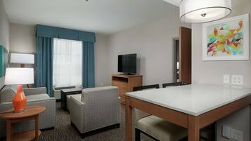 Quarto de hotel com mesa de jantar, dois sofás, televisão e abajur.