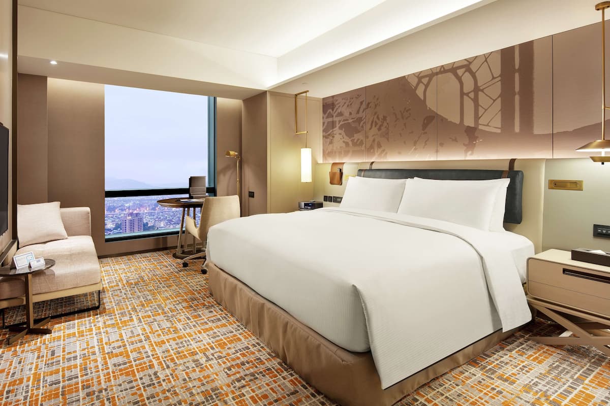 Quarto de hotel com uma cama grande, uma escrivaninha, uma cadeira e vista para a cidade.