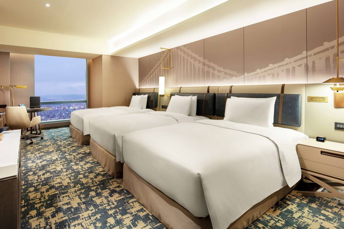 Quarto de hotel com duas camas, uma escrivaninha e vista para a paisagem urbana.