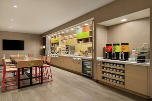 Uma cozinha moderna com área de refeições, equipada com cafeteira, geladeira e televisão de tela plana.