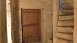 Um corredor de pedra estreito com uma porta de madeira e uma escadaria de pedra.