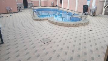 Piscina externa com deck revestido de azulejos, cercada por um muro baixo e uma cerca de arame farpado.