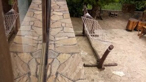 Um pátio com piso de pedra, uma rede e banquetas de madeira.