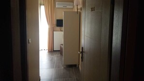 Um corredor com porta, radiador, televisão e janela com cortinas.
