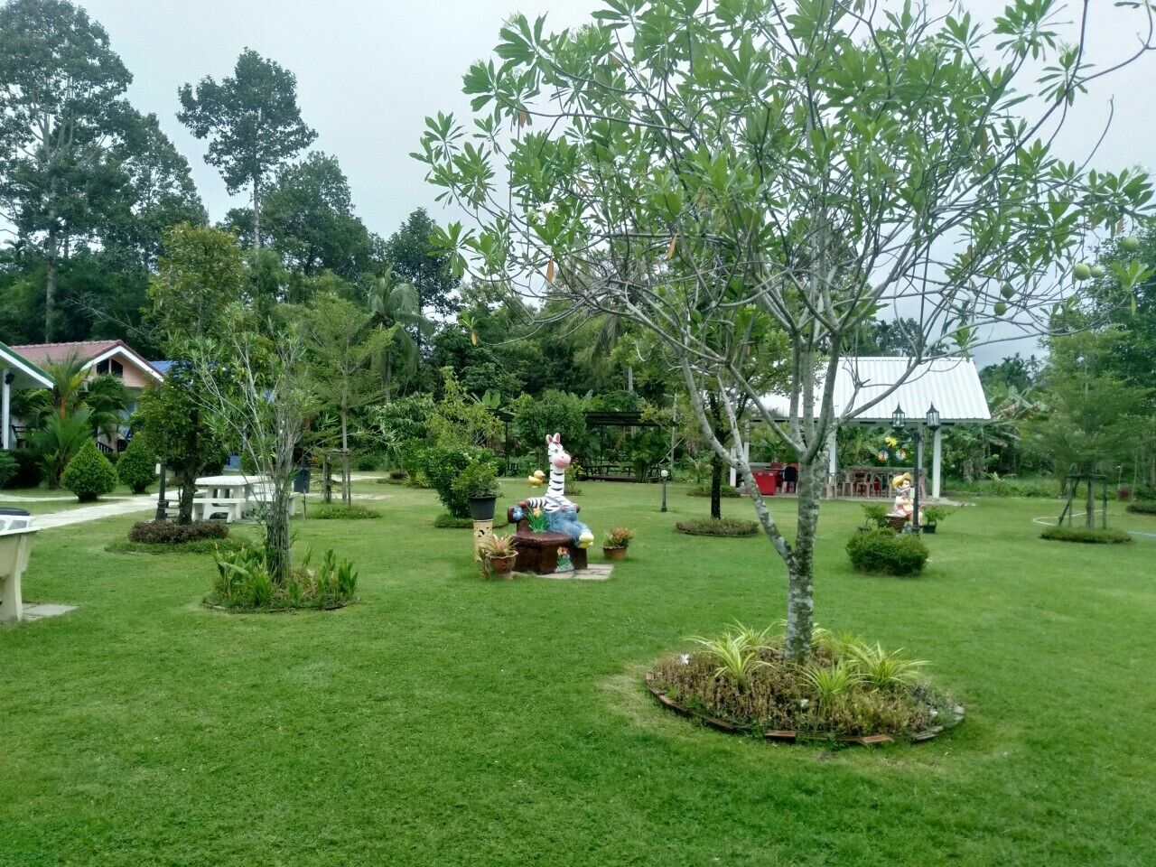 Um jardim bem cuidado com diversas árvores e arbustos, uma pequena estátua e um gazebo.