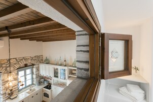 Uma cozinha com painel de parede de pedra, vigas de madeira e armários brancos.