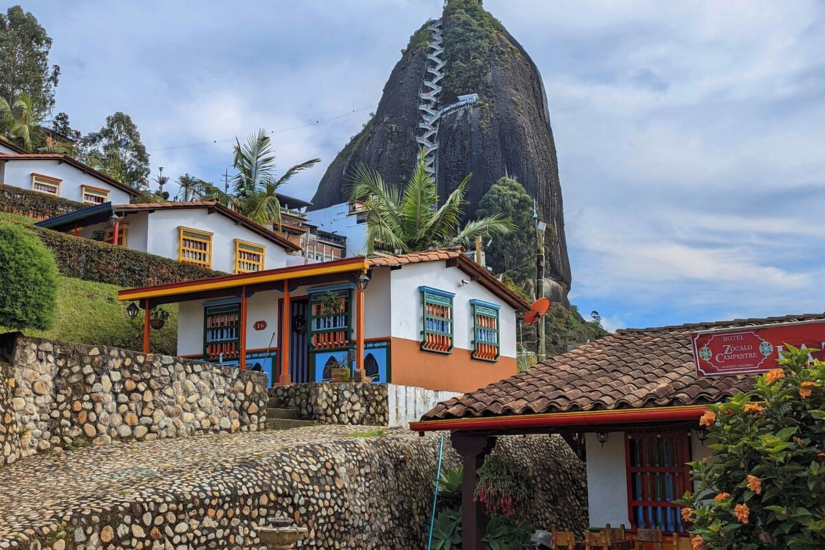 Hotel com parede de pedra e canteiros de flores coloridas na frente.