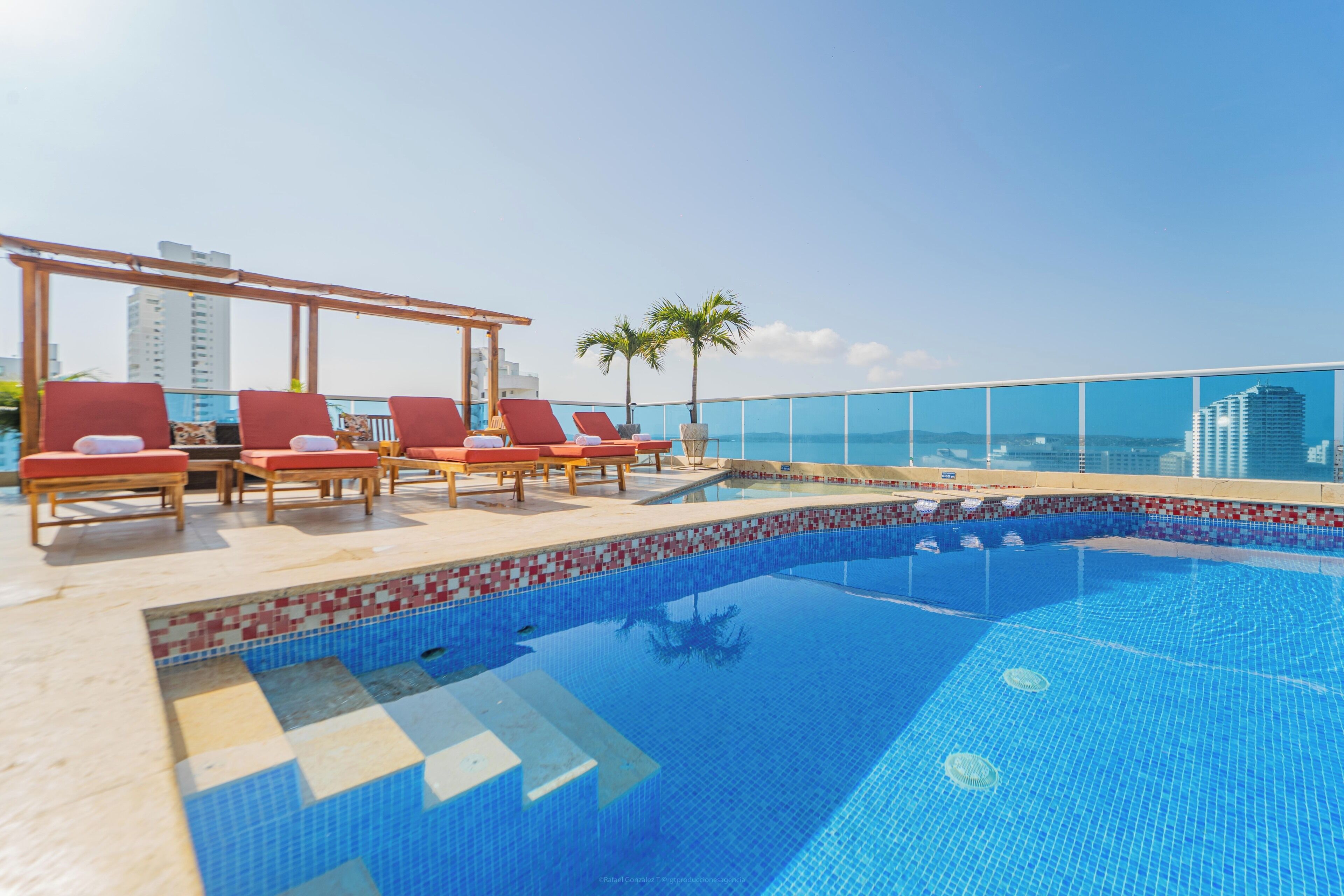 Uma piscina no terraço com espreguiçadeiras, um pergolado e vista para o horizonte da cidade.