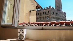 Vista de um edifício histórico com uma torre alta e janelas em arco, vista de uma varanda com um alto-falante e moldura de janela.