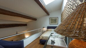 Quarto moderno estilo loft com teto de vidro, cama com cabeceira branca, sofá azul e abajur de vime.