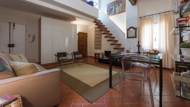 Uma sala de estar ampla com pé direito alto, uma escada, um espaço para refeições e uma estante de livros.