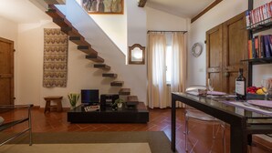 Uma sala de estar moderna com escada, área de jantar com mesa posta para dois e uma estante repleta de livros.
