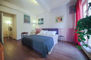 Quarto com cama, escrivaninha e cadeira. Há duas pinturas na parede.