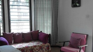 Um quarto com cama, uma cadeira e janela com persianas.