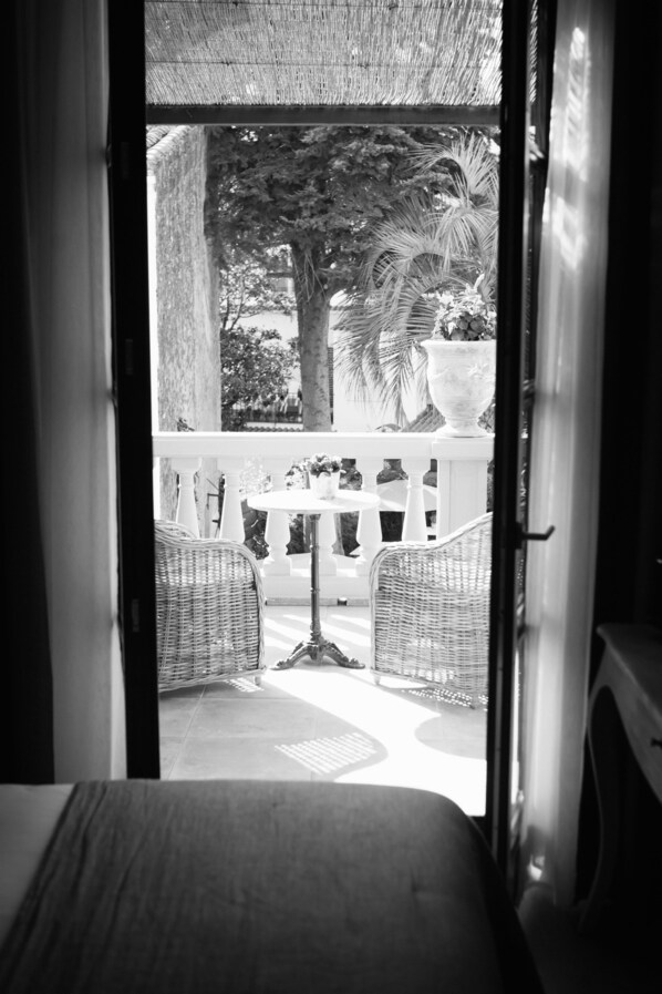 Vista de dentro de um quarto para uma varanda externa com mobiliário de vime e guarda-corpo branco.