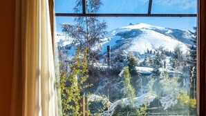 Uma cama com uma toalha enrolada e vista para uma montanha nevada através de uma janela.
