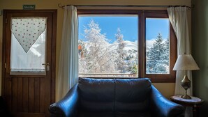 Quarto com sofá de couro, janela com vista para árvores cobertas de neve, luminária sobre uma mesinha de cabeceira e porta com placa indicando 