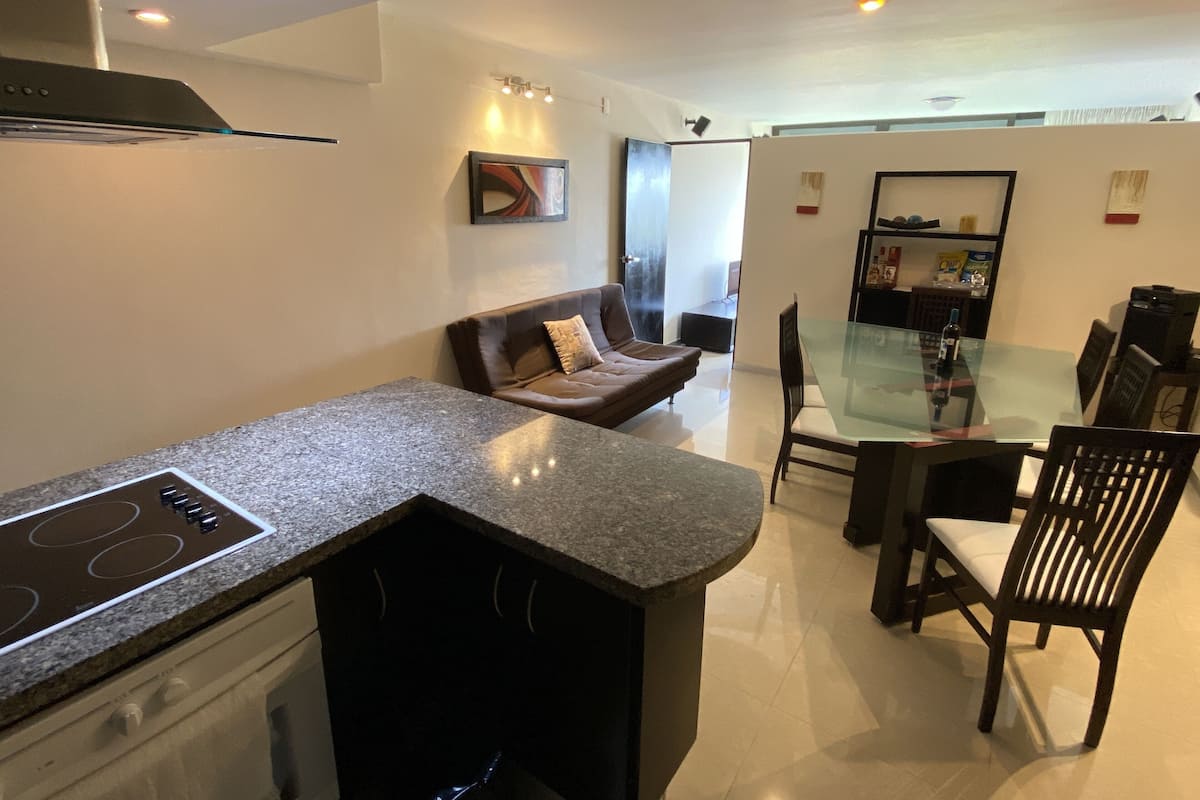 Cozinha moderna com bancada de granito, forno embutido e área de jantar com mesa e cadeiras de vidro.