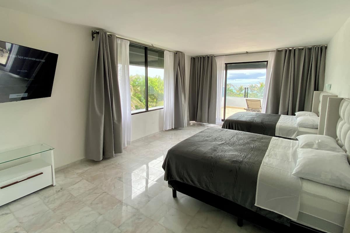 Quarto de hotel com duas camas, televisão na parede e varanda com vista para o mar.