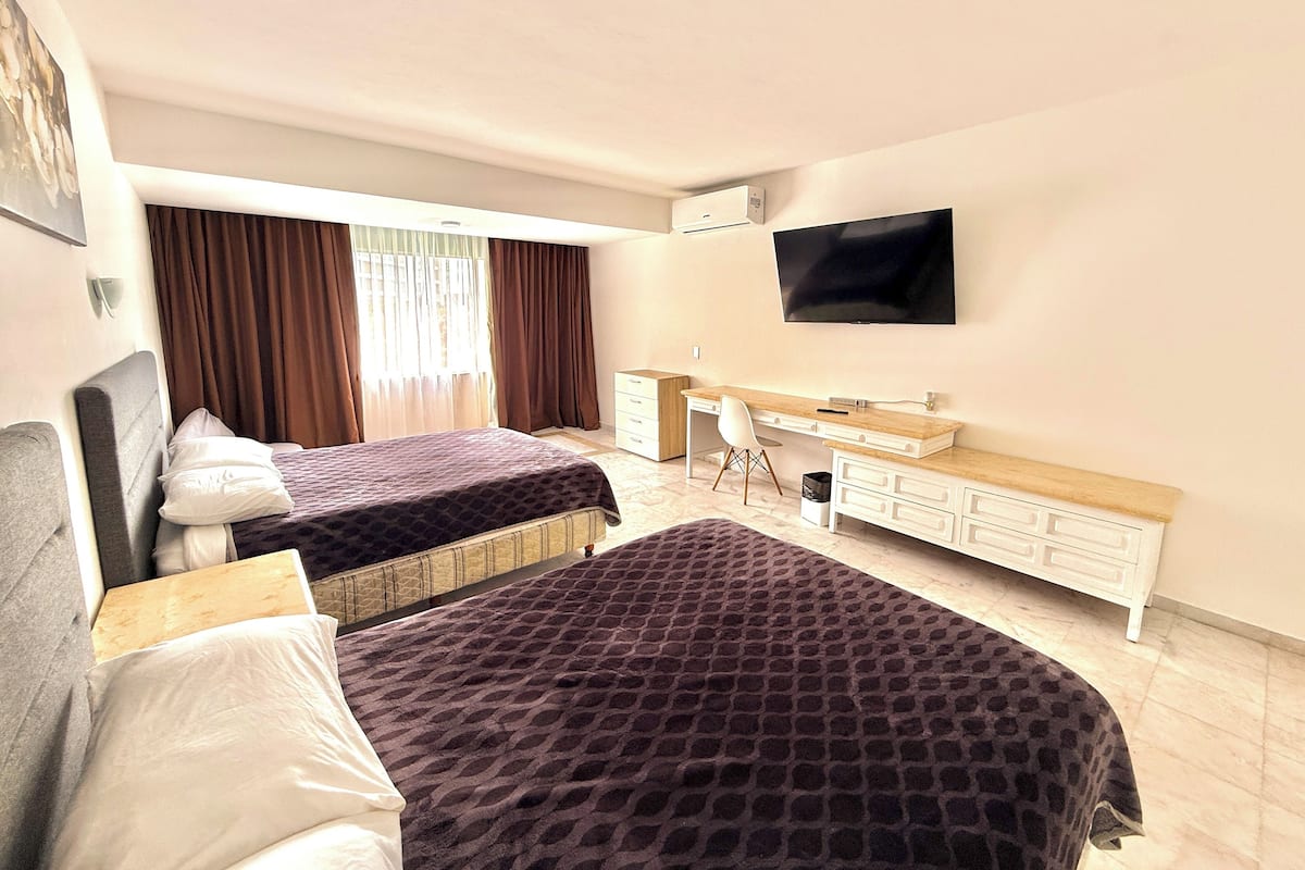 Quarto de hotel com duas camas, uma escrivaninha, televisão e janela com cortinas.