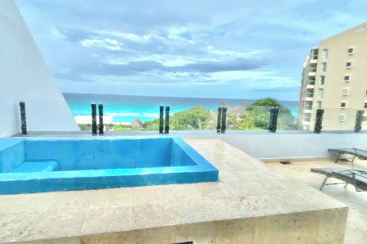 Piscina no terraço com vista para o oceano e um edifício ao fundo.