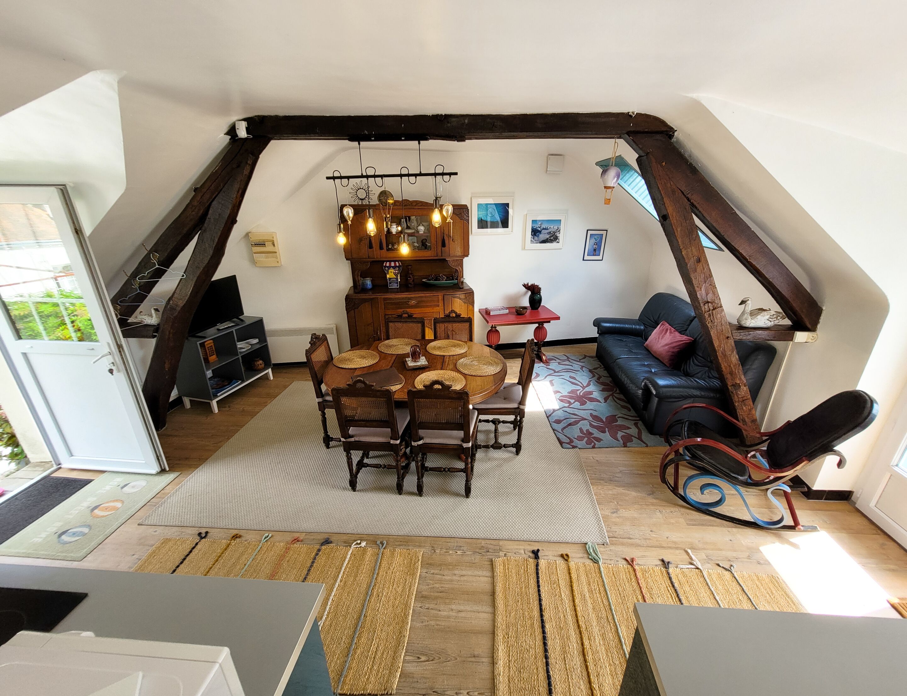 Um quarto de sótão acolhedor com uma mesa de jantar, cadeiras, um sofá e uma cadeira de balanço.