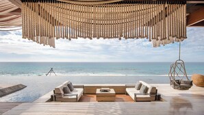 Um espaço de relaxamento à beira-mar com deck de madeira, cadeira suspensa e sofá voltado para o oceano.