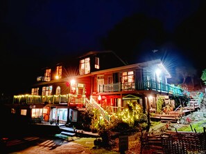 Uma casa de dois andares com varanda, alpendre e um jardim frontal bem iluminado.