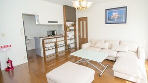 Uma sala de estar com sofá branco, mesa de centro de vidro e aparador de madeira com portas de vidro.