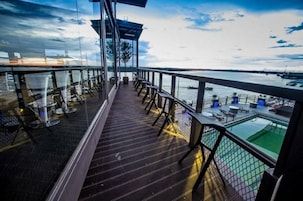 Um terraço com cadeiras e mesas, com vista para a água.