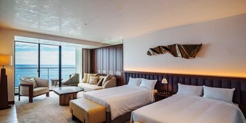 Quarto de hotel com uma janela grande, duas camas, área de estar e um detalhe decorativo na parede.