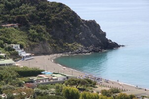 Vista costeira com praia, falésias rochosas e um edifício com telhado verde.